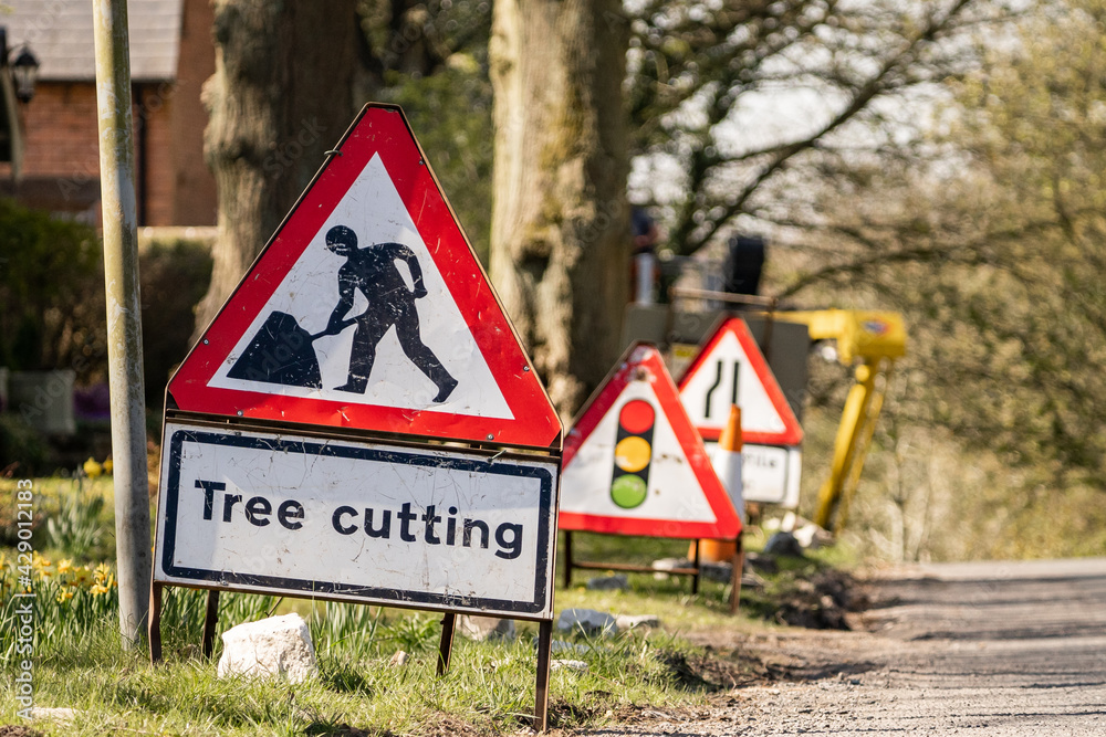 Red and white tree cutting warning signs standing at side of road with ...