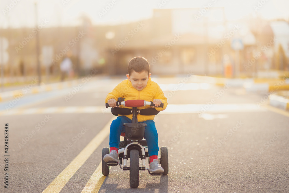 Happy three years old boy is riding a bike in an empty road during ...