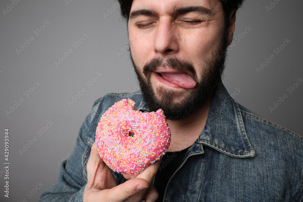 Hungry overweight bearded man eating donuts isolated on grey background ...