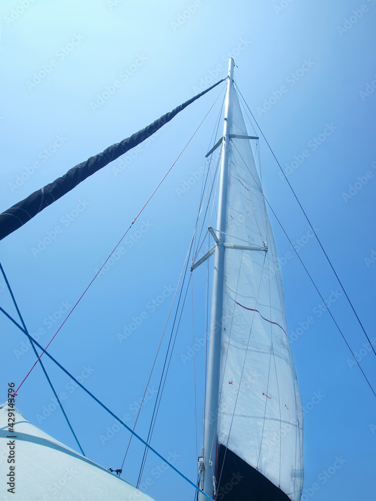 High mast, sail and wind on the background of a clear blue sky ...