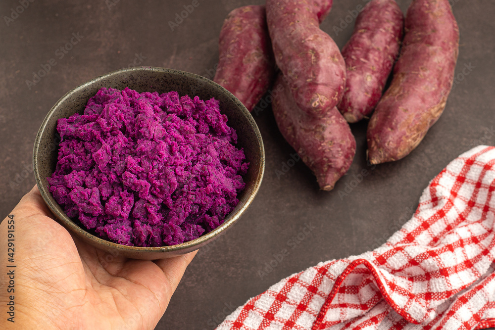 Hand holding of mashed purple sweet potatoes in a bowl with purple yams ...