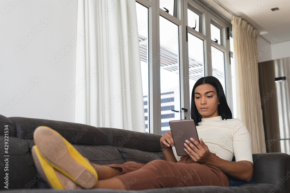 Mixed race transgender woman relaxing in living room lying on couch ...