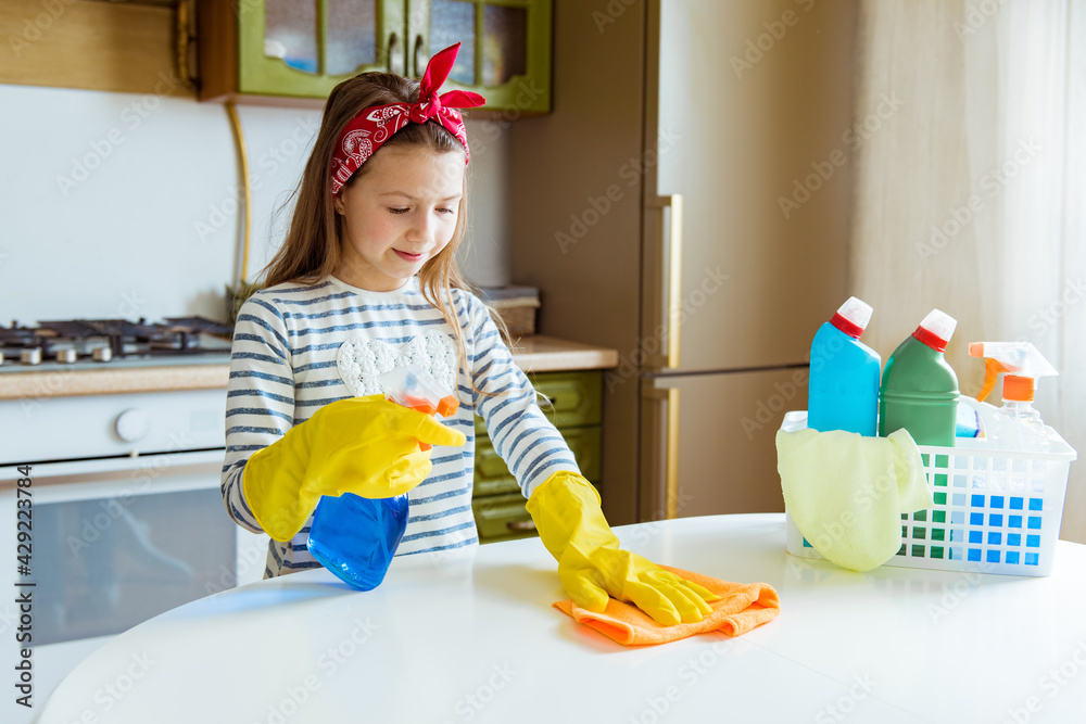 Positive child girl makes cleaning the kitchen table. Teenager rubs ...