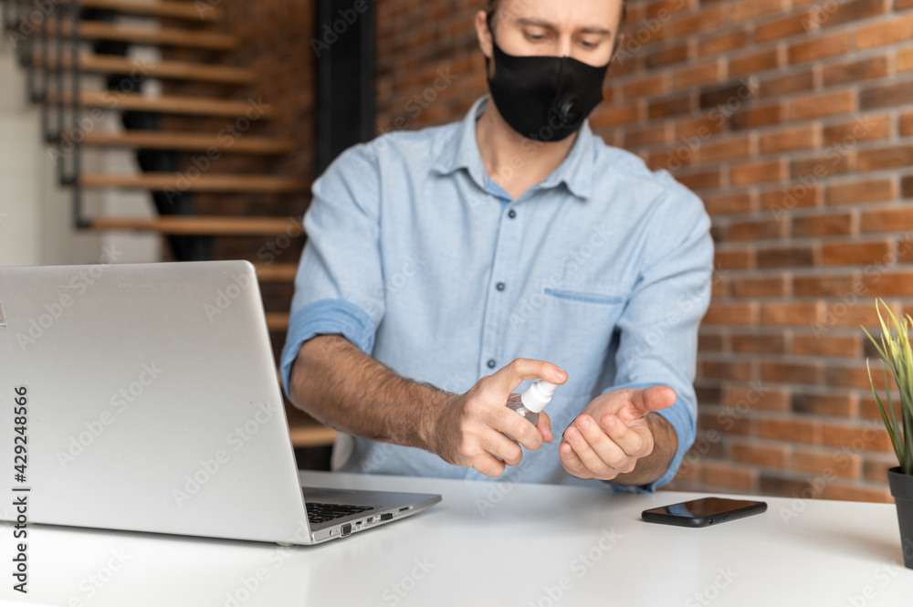An male office employee wearing mask is spraying antibacterial ...