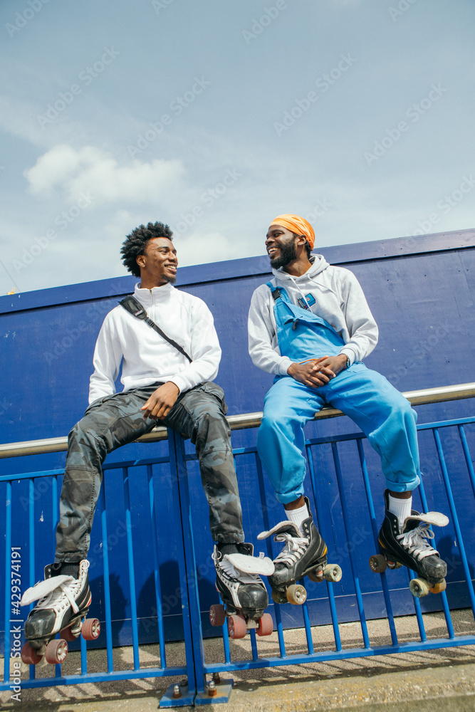Two friends wearing roller skates and sitting on railing and laughing ...