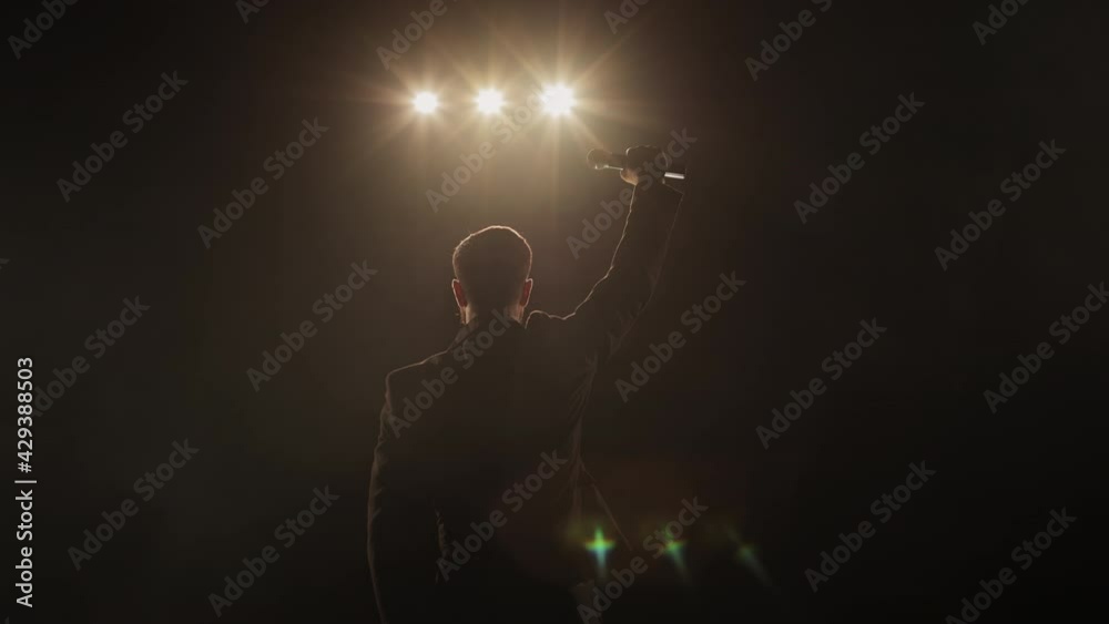 The man is standing on stage and raising up the microphone. He's ...