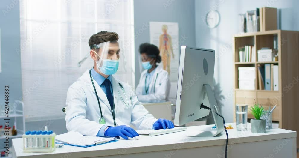 Portrait young Caucasian male doctor sitting in cabinet in medical ...