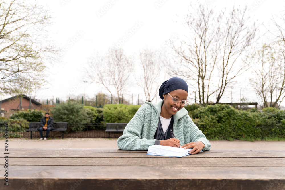 Black Muslim woman in park writing Stock Photo | Adobe Stock