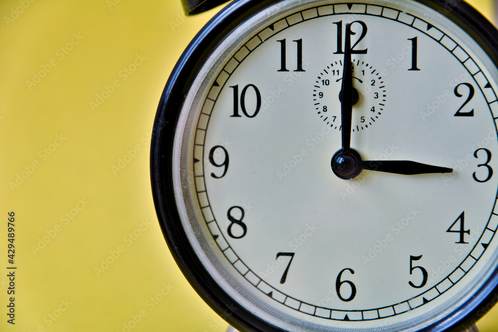 Shot of vintage retro analog clock on yellow background showing 3 o ...