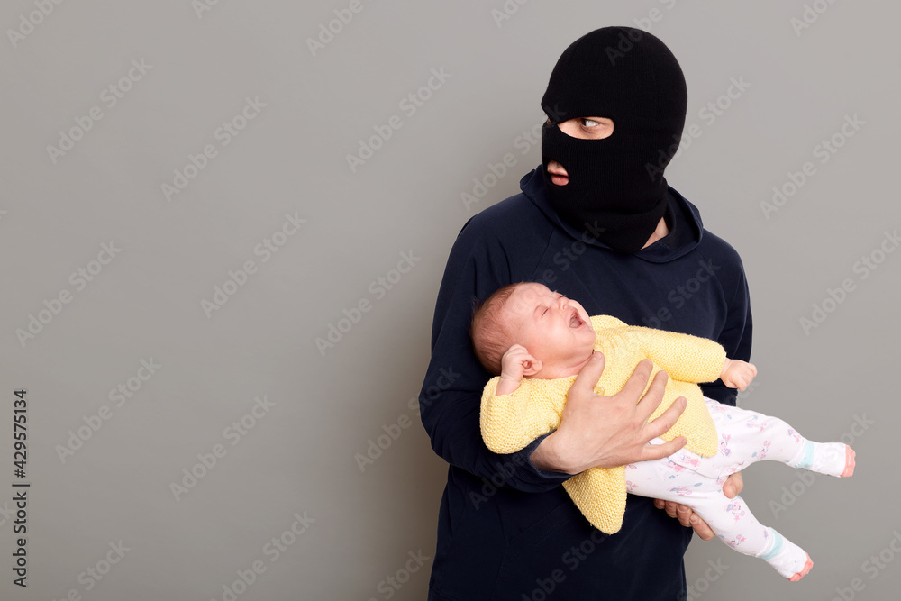 Man thief in balaclava kidnapped newborn crying baby, runs away, looks back while holding child ...
