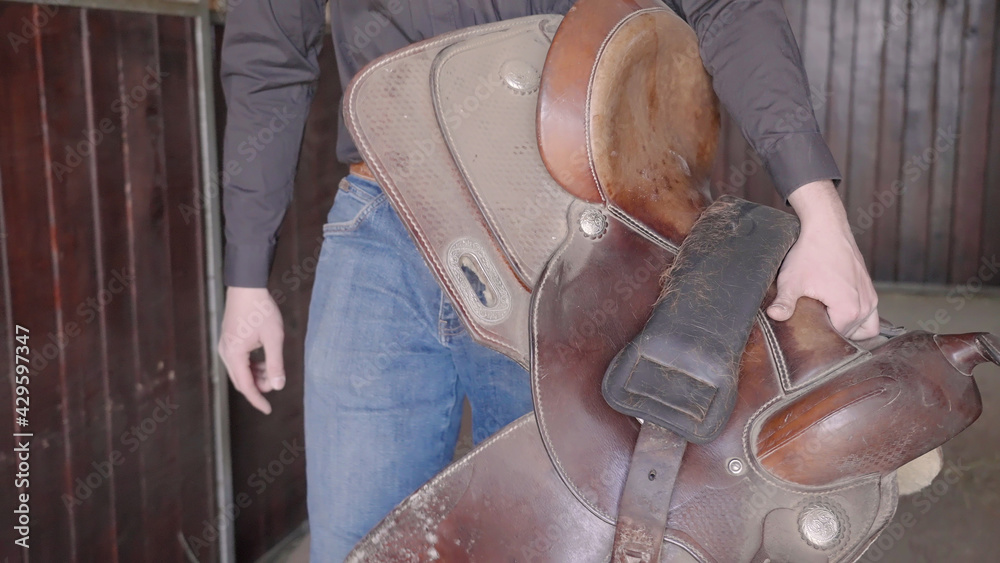 Cowboy carry western saddle under arm from barn Stock Photo | Adobe Stock