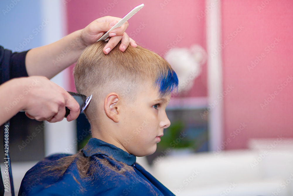 Foto de A little cute boy sits in a hairdresser's at a stylist's, a ...