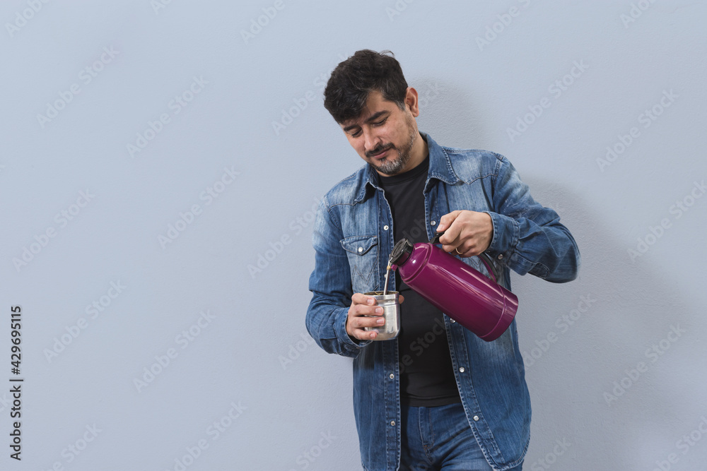Hombre cebando mate con termo color bordó vestido con denim en fondo ...