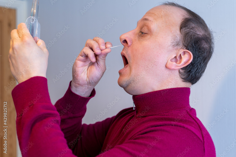 Man using a Covid-19 Rapid Lateral Flow Test swab in his nostril whilst ...