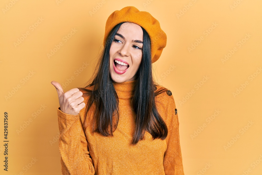 Young brunette woman wearing french look with beret pointing thumb up ...