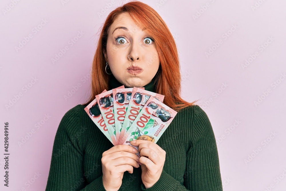 Beautiful redhead woman holding 100 new zealand dollars banknote ...