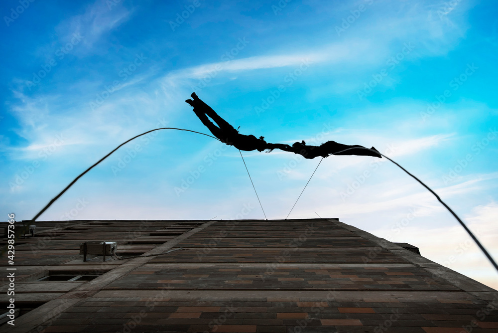 Two person silhouettes, dancing in the air, tied by the ropes on the ...