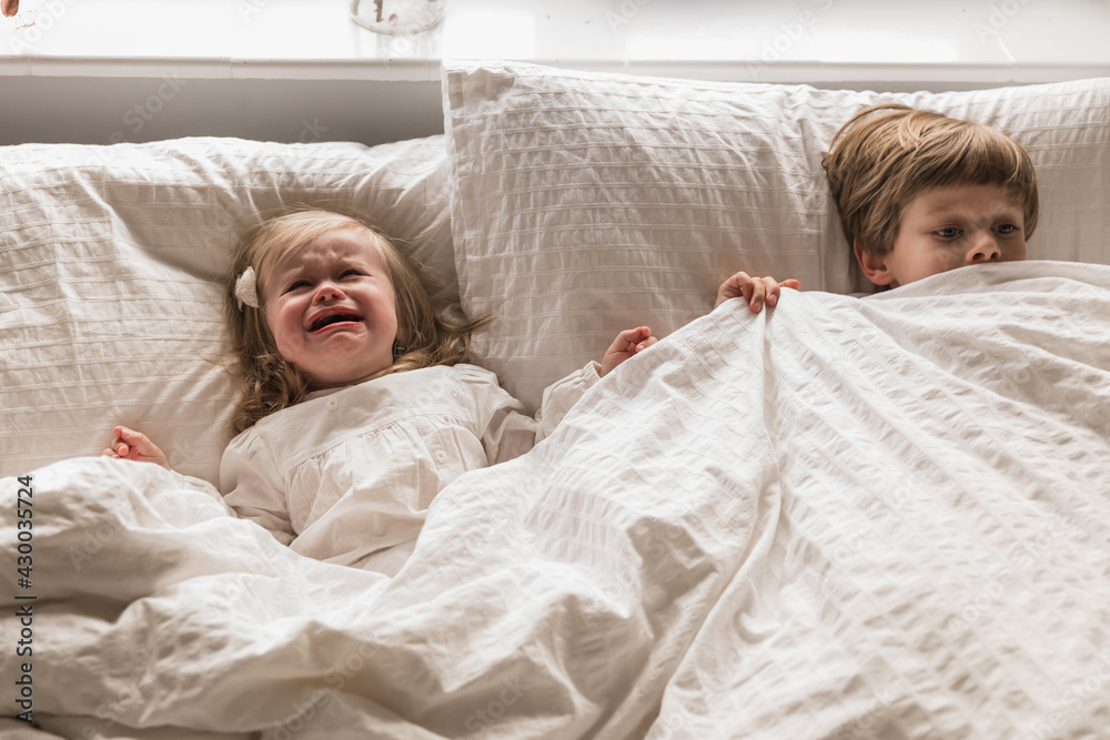 Picture of two siblings. The boy is lying in bed with his little sister ...