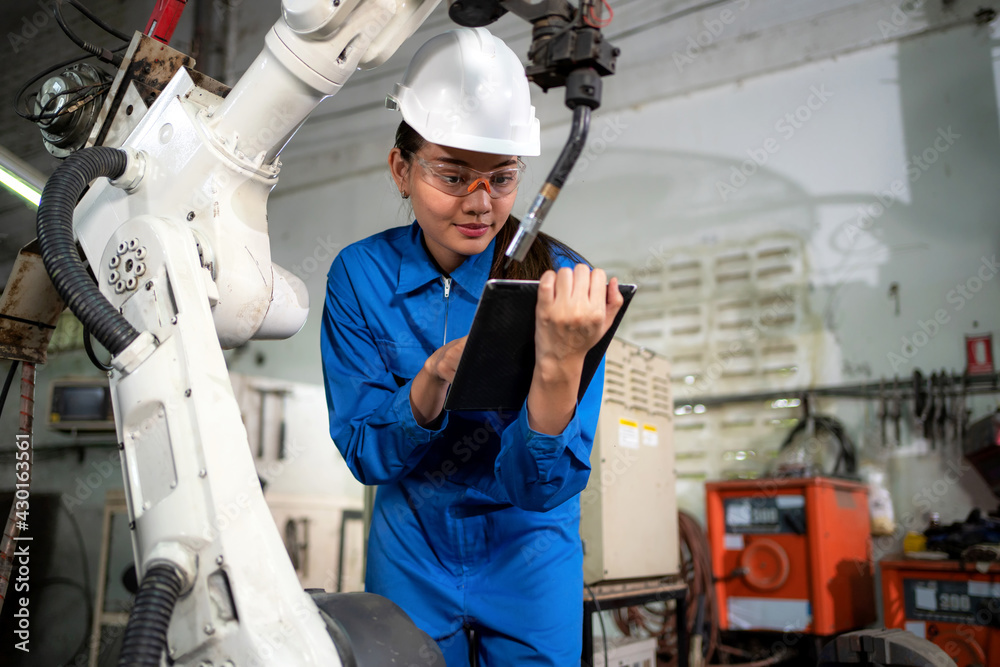 Engineer woman looking at tablet and see how to operate robotic arm ...