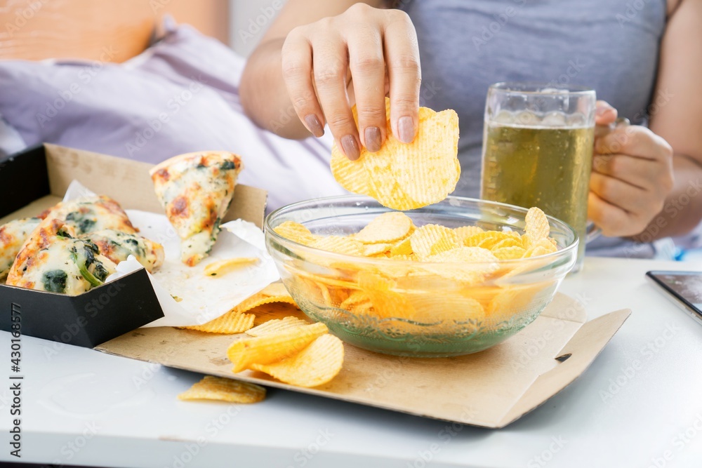 unhealthy woman hand eating potato chips, pizza and drinking beer in ...