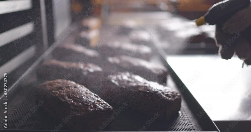 Fresh hot bread comes out of the oven on a conveyor belt. Baker is ...