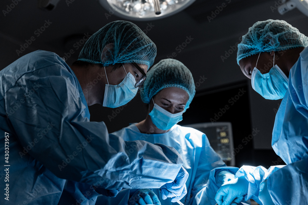 Diverse group of male and female surgeons in operating theatre wearing ...