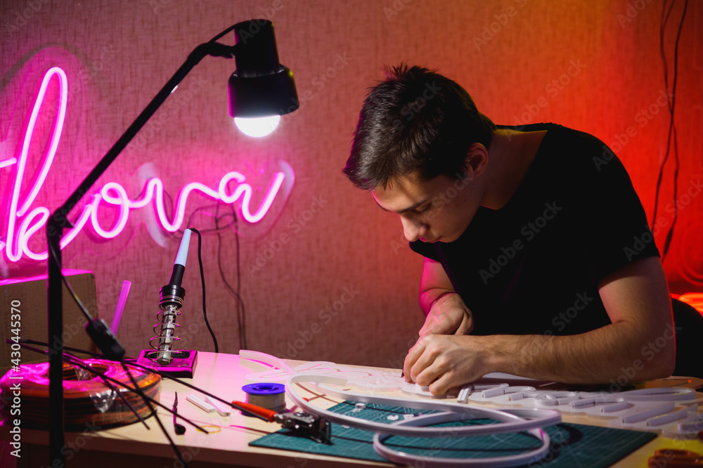 Young craftsman working with acrylic signboard and flex neon in studio ...