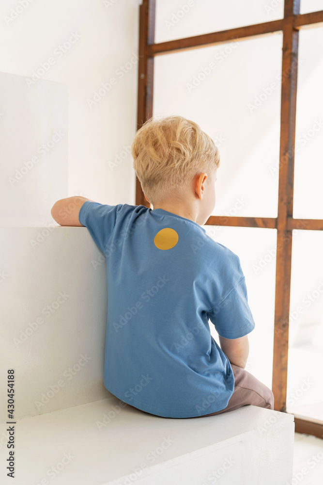 little boy with blond hair, sitting with his back turned away from ...