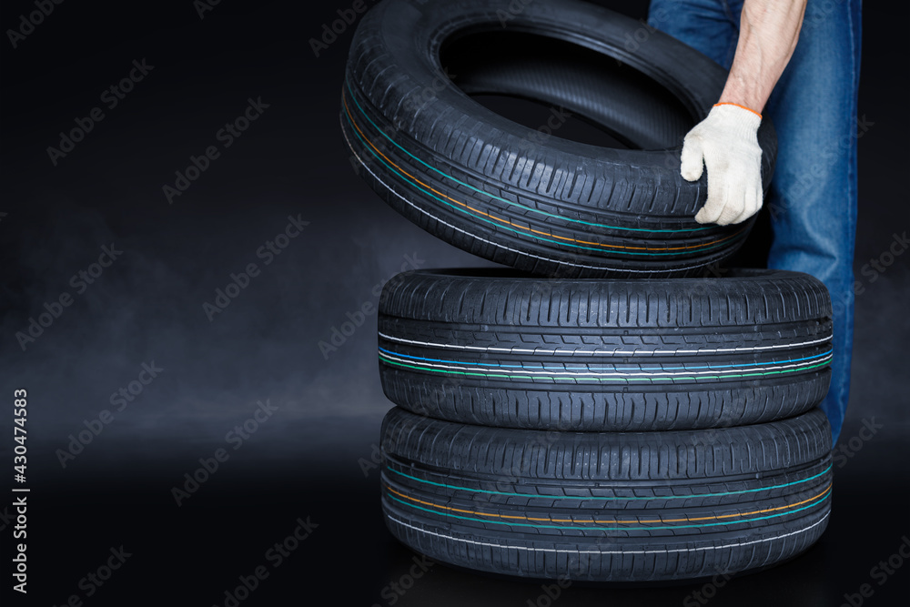 Man puts a tire in a stack of tires on creative black background. Tire ...