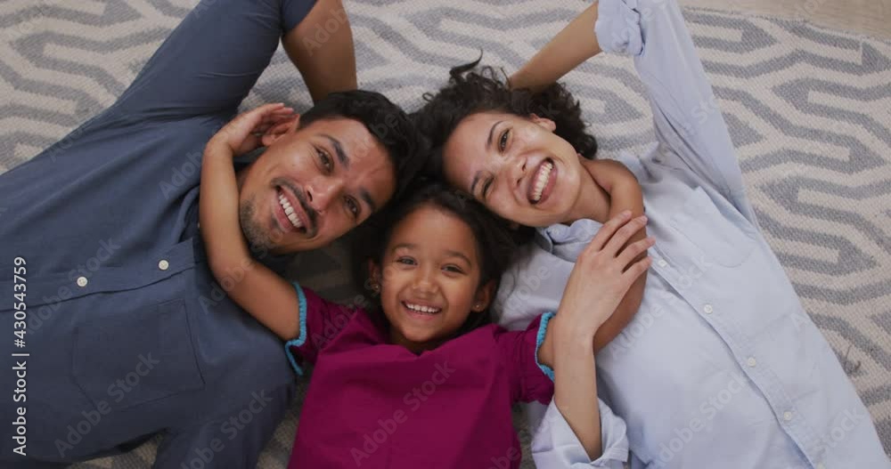 Happy hispanic parents and daughter embracing lying on floor in living ...