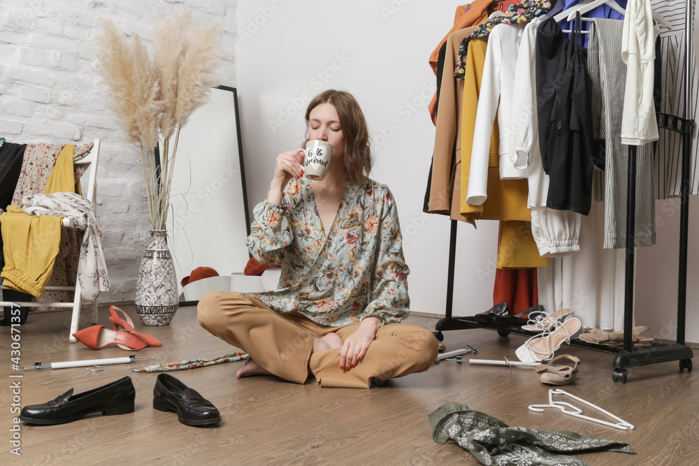 Stressed young woman sitting in the messy room full of clothes. Nothing ...