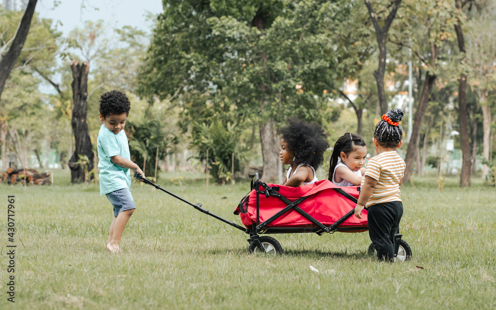 Mixed race little cute children pull and drag a red cart while playing ...