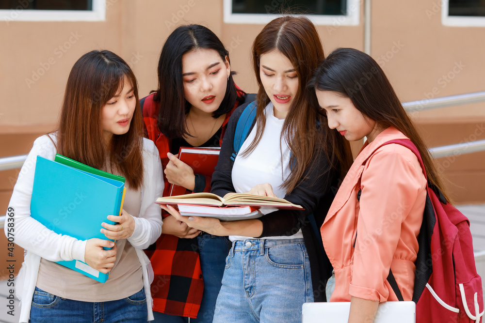 Group of four college student girls holding books standing and reading ...