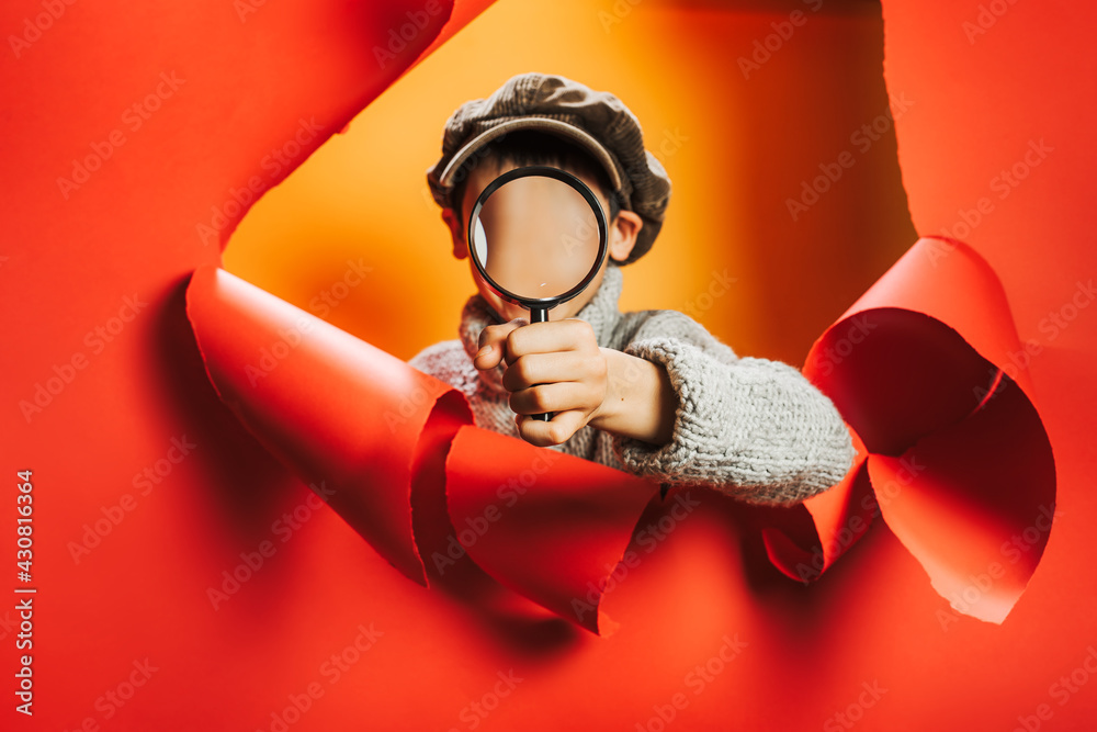 Boy holds magnifying glass that covers his face. Color torn paper wall ...