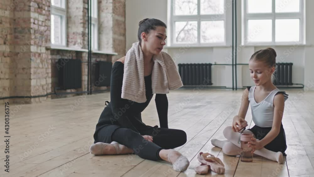 PAN shot of beautiful young ballet teacher and little girl sitting on ...