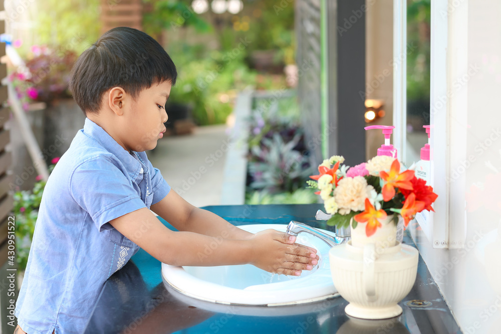 An Asian young boy washing his hand at an outdoor faucet sink and water ...