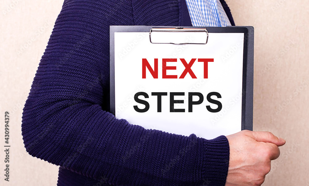 NEXT STEPS is written on a white sheet held by a man standing sideways ...