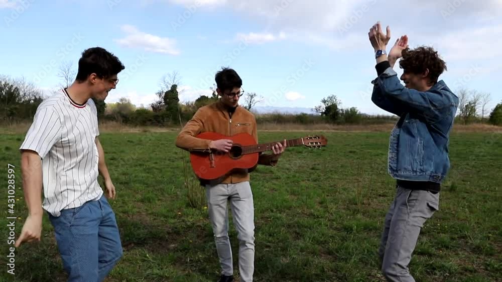 three friends in a meadow sing, play the guitar and dance happily ...