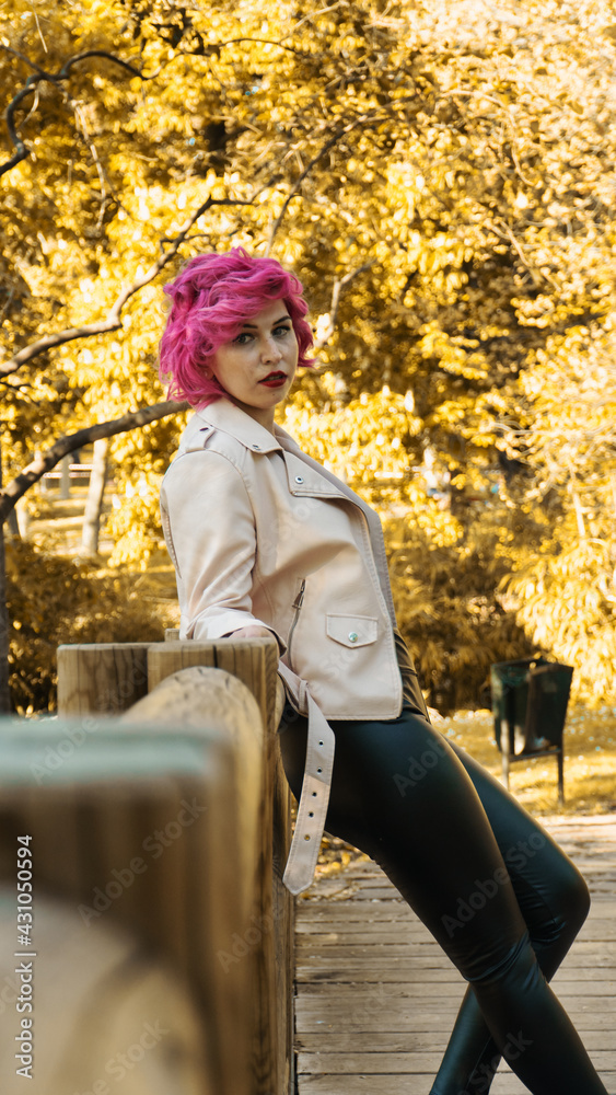 Mujer joven de pelo rosa apoyada de espalda a la baranda en el parque ...