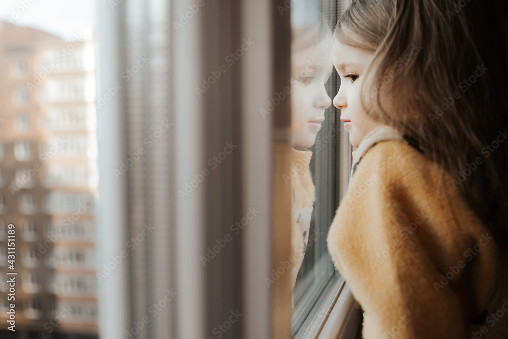 little girl looks out the window of a high-rise building in a sleeping ...