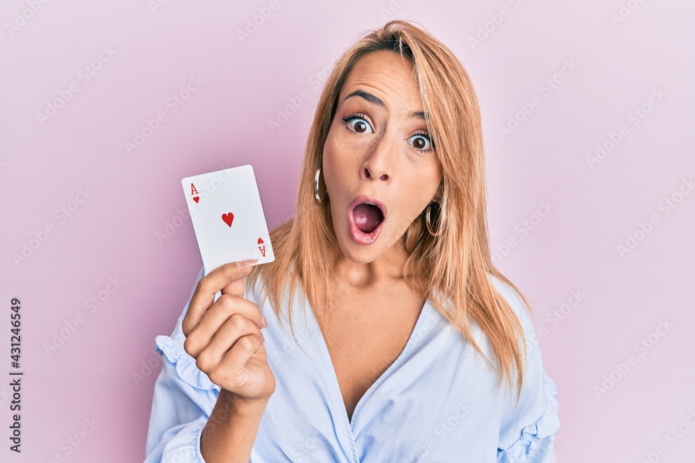 Beautiful blonde woman holding ace poker card scared and amazed with ...
