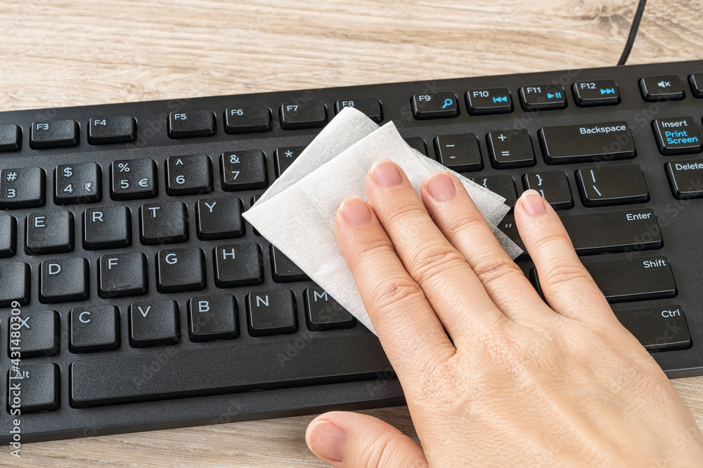 Woman hand wiping the black pc keyboard with a wet disinfecting wipe ...