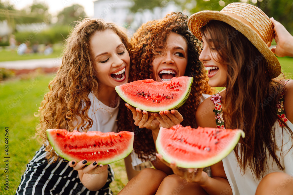 Three young having fun eating watermelon In the park. Young friends ...
