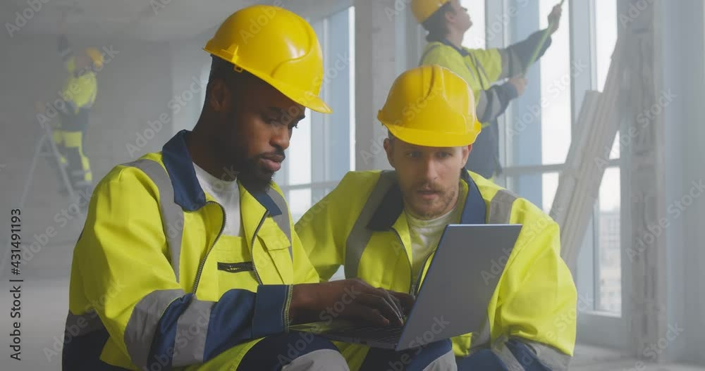 Portrait of two diverse builders reading plan of building on laptop ...