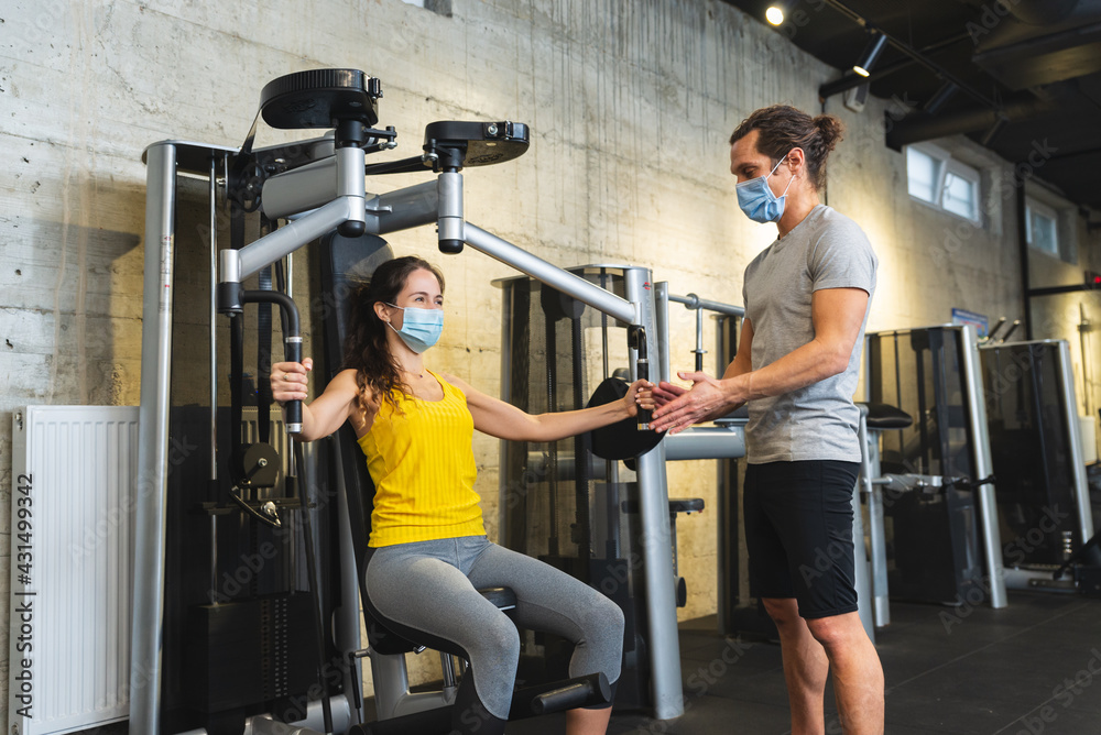 Personal trainer helping young female athlete in the gym while both of ...