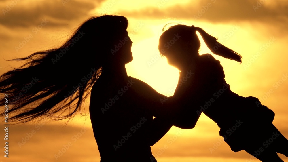 mom is circling her beloved healthy little daughter in her arms. silhouette of mom and baby at ...