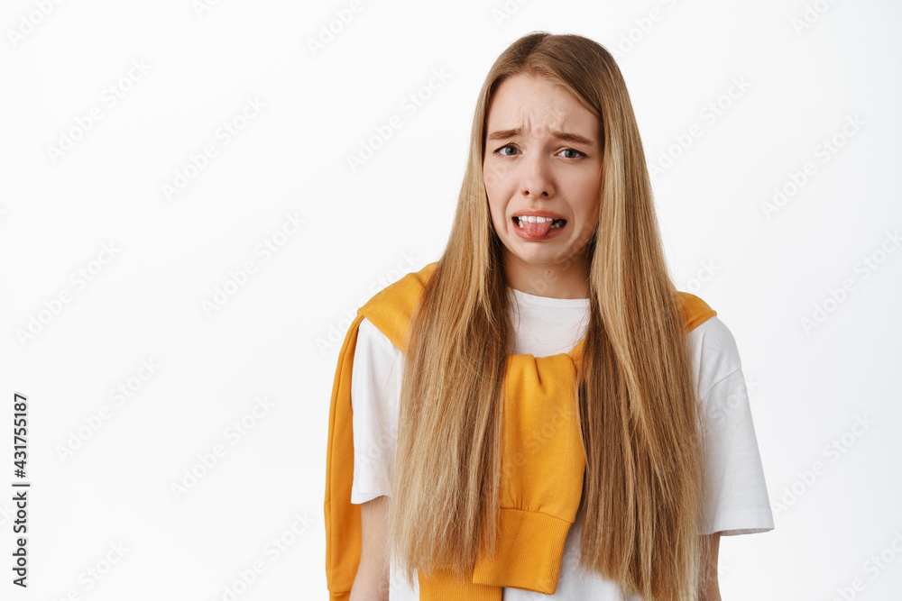 Blond young woman feeling disgusted, showing tongue and grimacing from ...