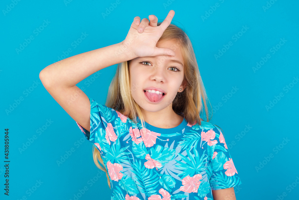 Funny Caucasian kid girl wearing hawaiian T-shirt against blue wall ...