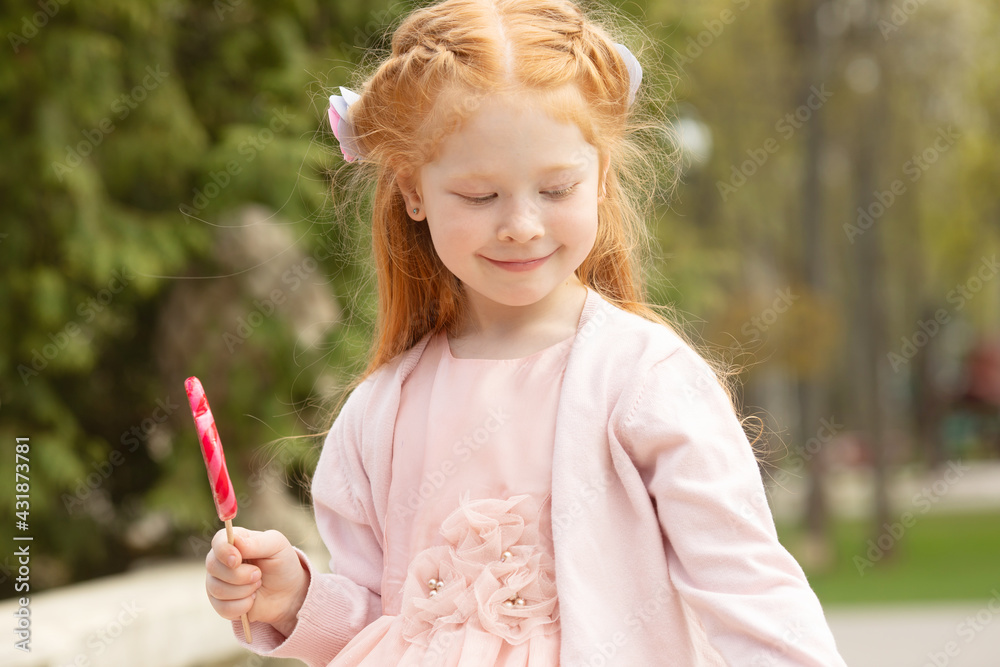 Cute little red hair girl eating huge heart-shaped lollipop outdoors on ...
