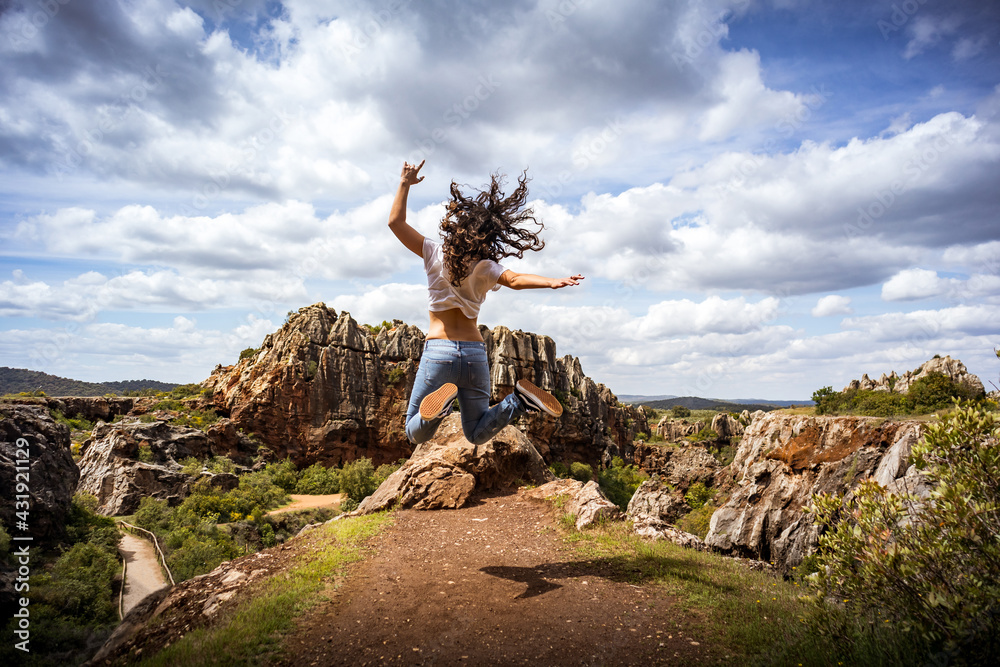 Girl jumping with arms outstretched in a spectacular natural mountain ...